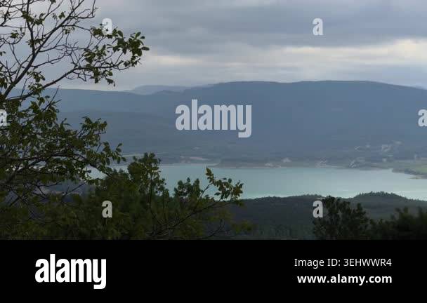 Overcast landscape with green leaves, a misty valley, calm lake, and ...
