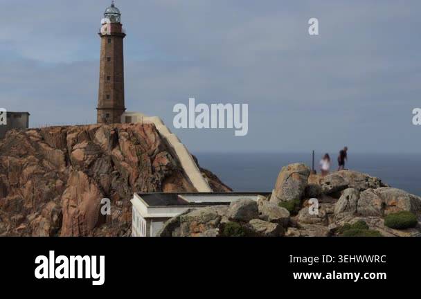 Red lighthouse on rocky cliffs two people watch the calm sea beneath a ...
