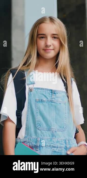 Pretty schoolgirl with loose long hair standing near school building ...