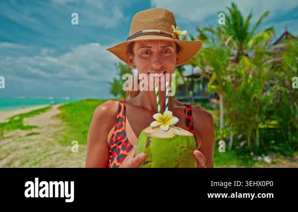 A close-up portrait of a woman drinking a fresh coconut cocktail with ...