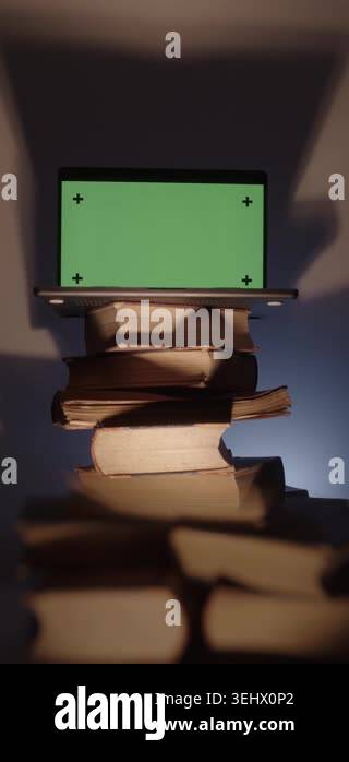 Laptop with green screen over stack of old books. Flashing light behind ...