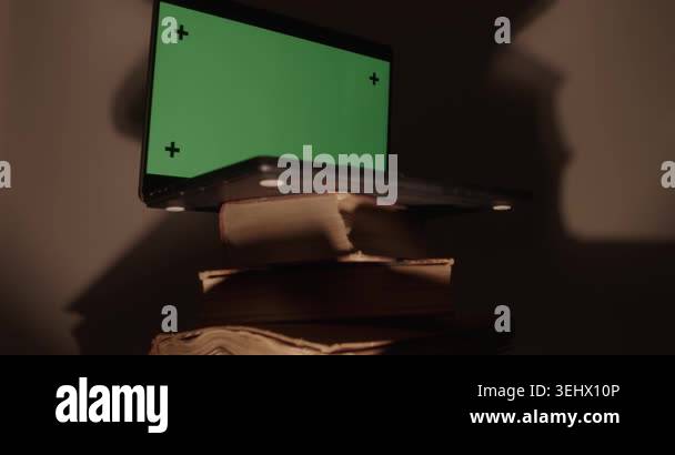 Laptop with green screen over stack of old books. Flashing light behind ...