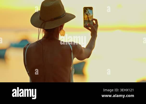 A girl in a white sundress and hat takes a picture of an incredibly ...