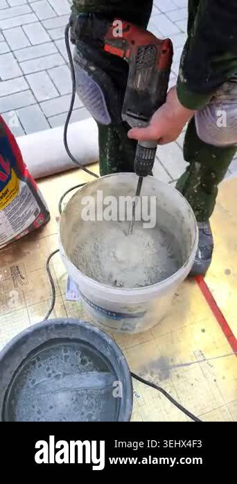 A builder uses an electric drill-mixer to mix gray cement mortar for ...