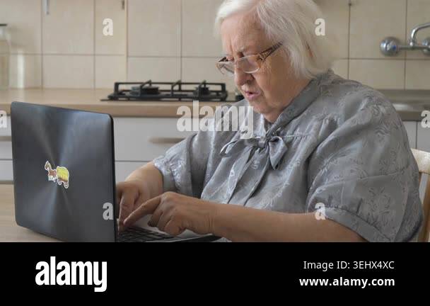Excited old woman is using laptop computer in a kitchen. Funny Stock ...
