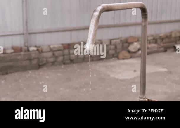 Water drips slowly from the threaded end of a weathered metal pipe ...