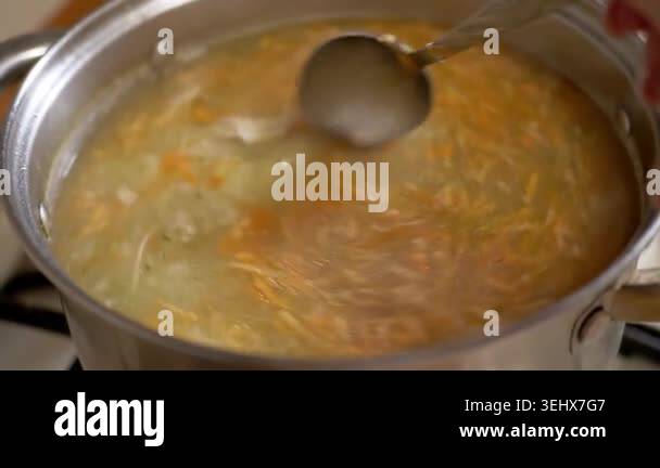 Close-up of a metal ladle stirring a steaming pot of homemade chicken ...