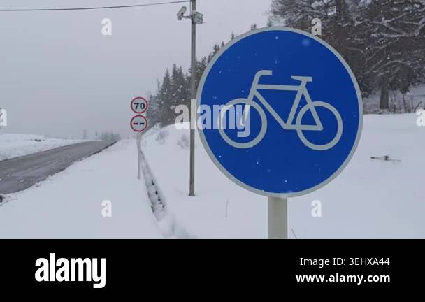 Blue bicycle lane road sign on a country road during a winter snowstorm ...