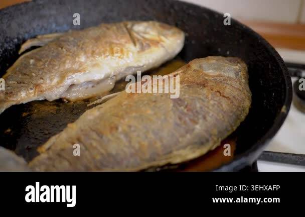 Close up, two fish are frying in a pan, displaying an enticing golden ...