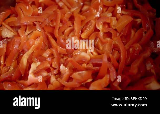 Freshly chopped red bell peppers simmer gently in a pot, highlighting ...