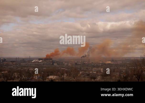 A massive factory releases thick toxic orange smoke into the overcast ...