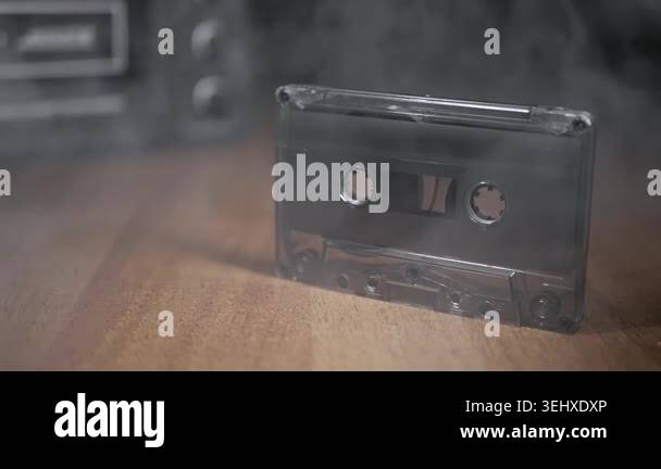 A transparent audio cassette rests on a wooden desk as thick cinematic ...