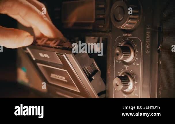 A hand inserts an analog audio cassette tape into a vintage stereo deck ...