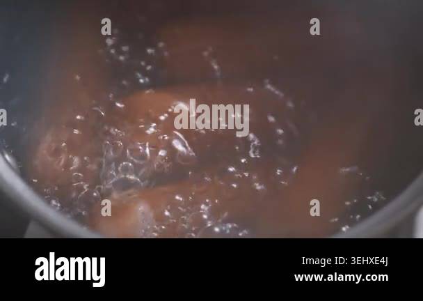 Close-up of plump hot dogs boiling vigorously in a metal pot full of ...