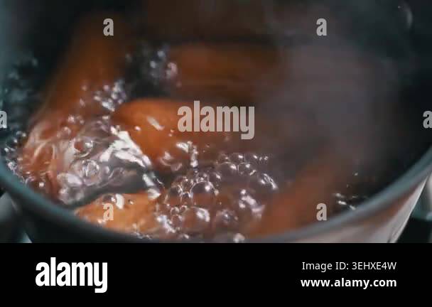 Thick brown sausages boil vigorously inside a dark pot of bubbling ...