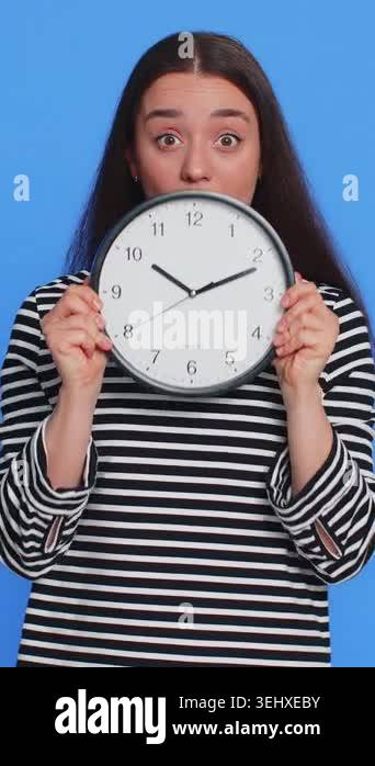 Serious strict Caucasian woman holding office clock hiding behind ...