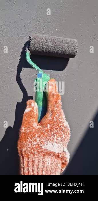 POV shot of a gloved hand using a paint roller to apply grey paint to a ...