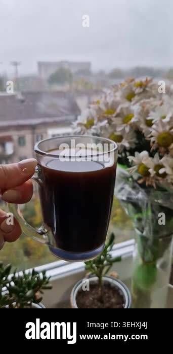 Vertical close-up shot of a hand holding a clear glass mug filled with ...