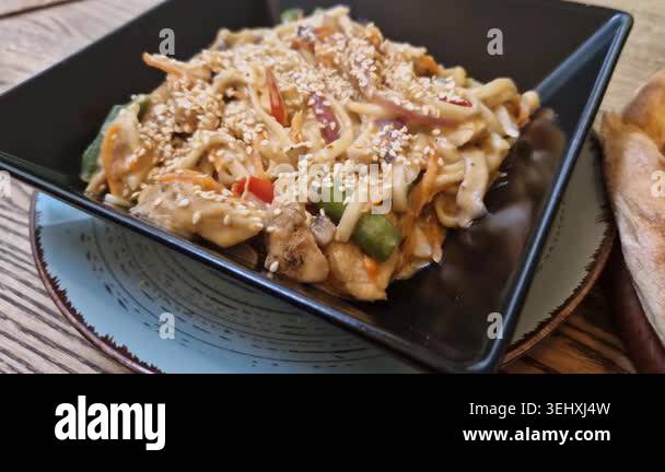Close-up shot of a steaming bowl of chicken noodle stir-fry, topped ...