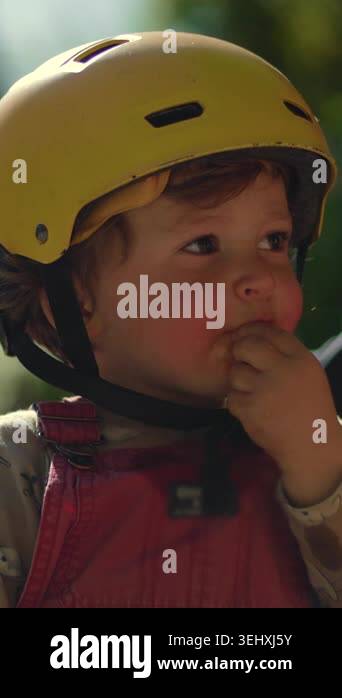 Young child in protective helmet eats fresh tangerine outside, showing ...