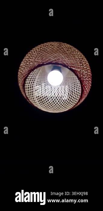 Handcrafted bamboo lampshade with a glowing light bulb hangs in a dark ...