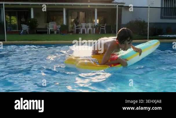 Boy attempting to stand upright on inflatable float in backyard pool ...