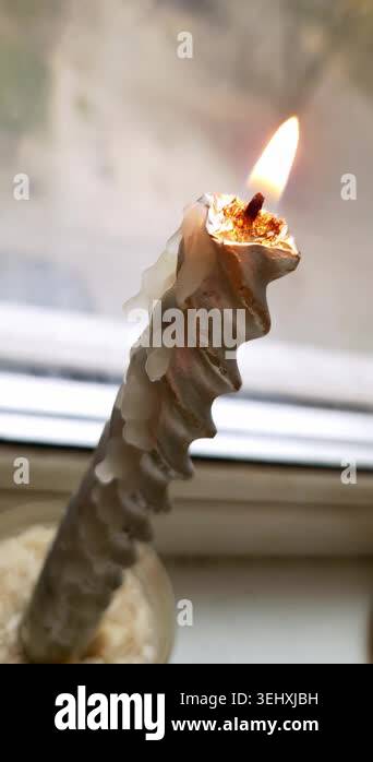 Spiral candle burns with a steady, flickering flame as melted wax drips ...