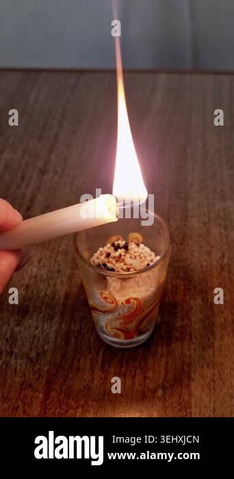 Vertical, close-up shot of a hand lighting a new white candle from an ...