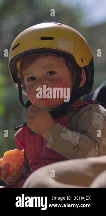 Young child in protective helmet enjoys fruit snack outside, expressing ...