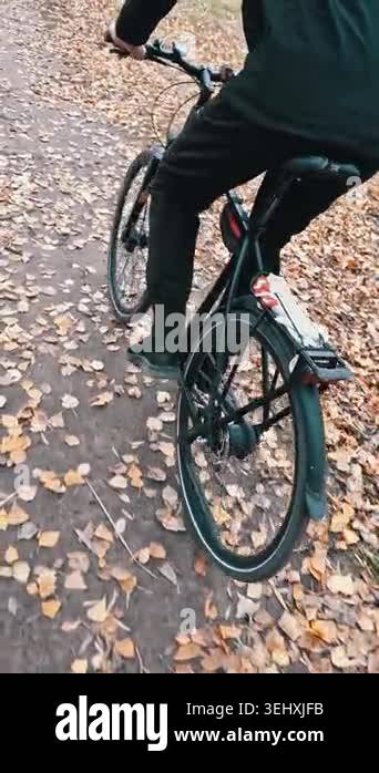 Man wearing all black rides a bicycle on a park trail covered in dry ...