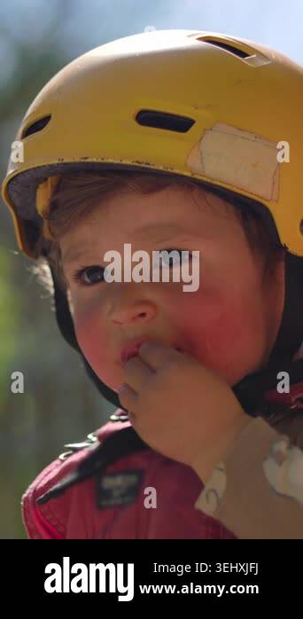 Young child in protective helmet snacks on fruit outside, showing ...