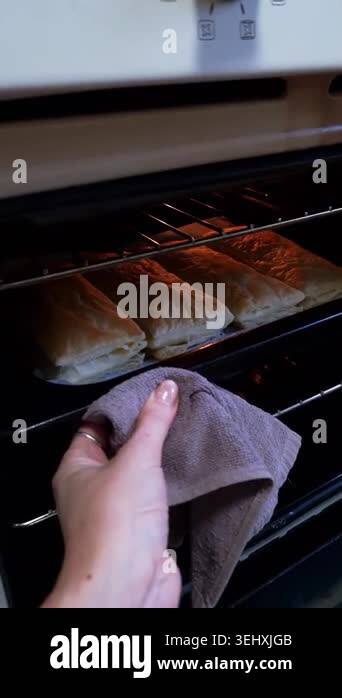 Female hand holds an oven door handle, revealing golden puff pastries ...