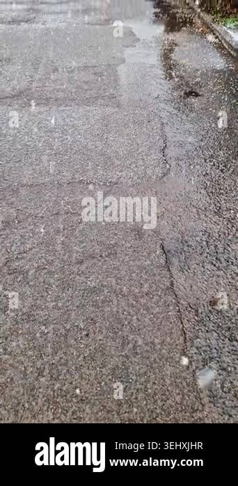Snowflakes fall and melt on a wet, cracked asphalt street during the ...