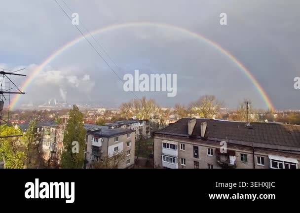 A vibrant full rainbow creates a colorful arc over an urban cityscape ...