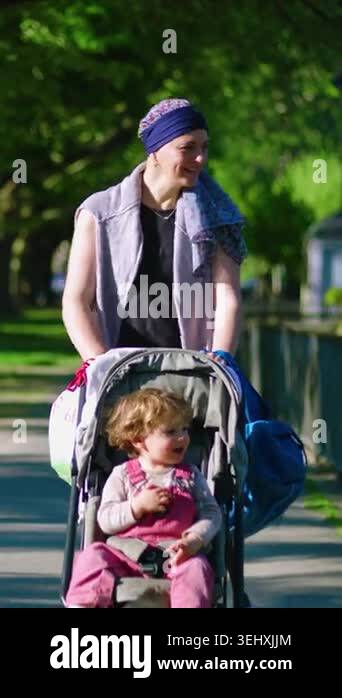 Mother wearing headscarf walks with child in stroller through tree ...
