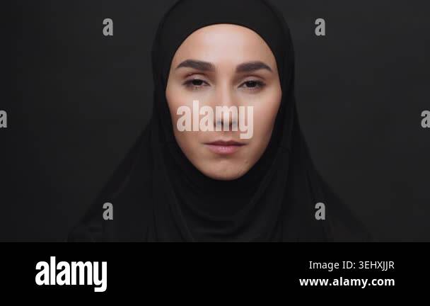 A close-up of a woman wearing a hijab. She has a serious expression and ...