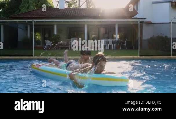 Two boys playing in swimming pool at sunset, one pushing the other off ...