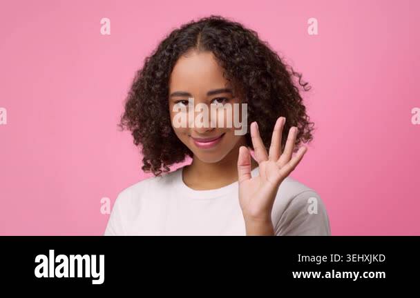 A young woman with curly hair smiles and raises her hand to show a ...