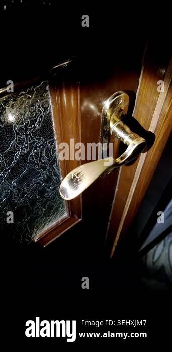Brass doorknob on a wooden door is illuminated by a moving light in a ...