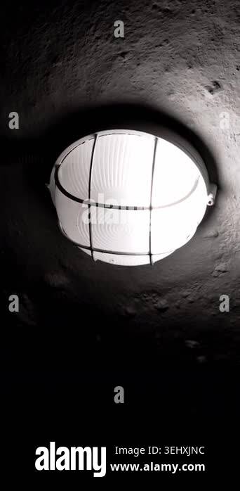 Old industrial bulkhead light with a protective cage flickers on a ...