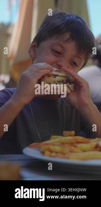 Young child carrying large burger at outdoor cafe table highlighting ...