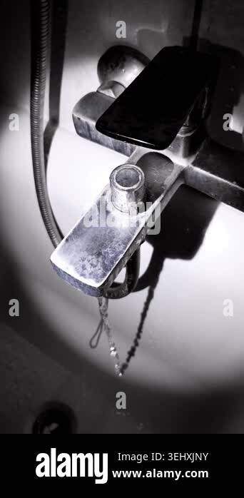 A close-up view captures an old, stained bathtub faucet steadily ...