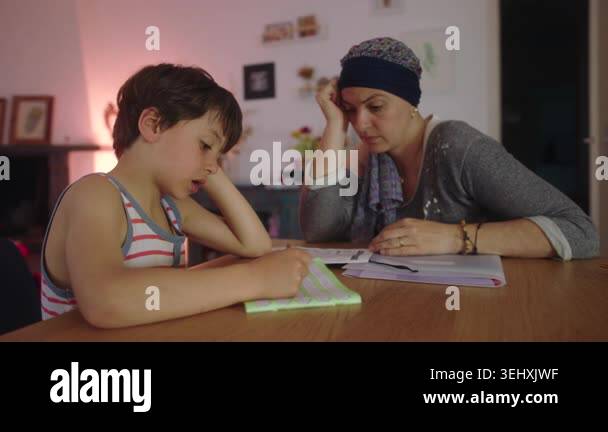 Mother in cancer treatment assisting child with homework indoors, calm ...
