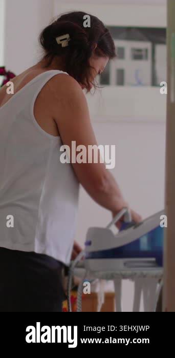 Female adult smooths clothing with iron during calm housekeeping moment ...