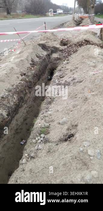 A deep earthen trench runs alongside a paved road at an active ...