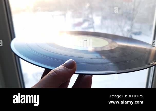 Detailed close-up: hand holding a black vinyl record. Bright sunlight ...
