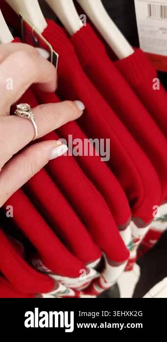A woman's hand examines a rack of red knitted Christmas sweaters in a ...