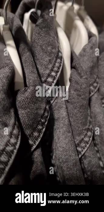 Dark grey denim shirts hang in a row on white plastic hangers on a ...