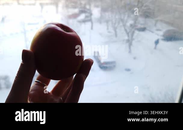 Woman's hand holds red apple indoors, against a blurred, out-of-focus ...