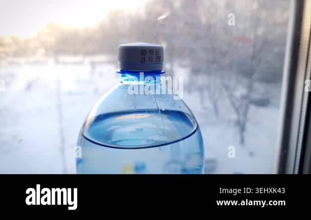 A plastic water bottle filled with rippling water rests on a windowsill ...